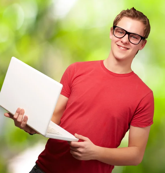 Portrait of young student man holding laptop against a nature ba ...